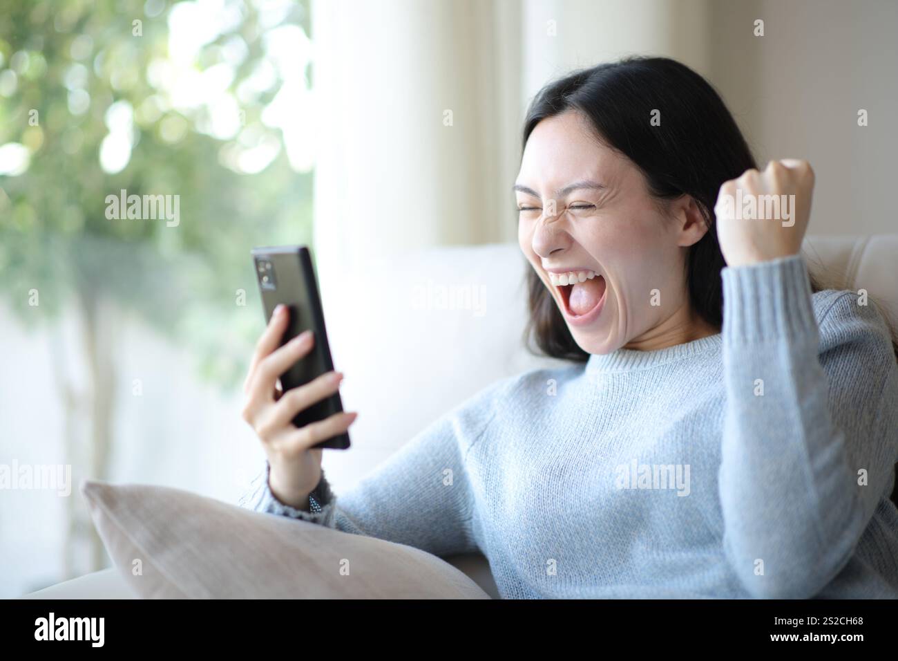 Excited asian woman celebrating success checking phone sitting on a ...