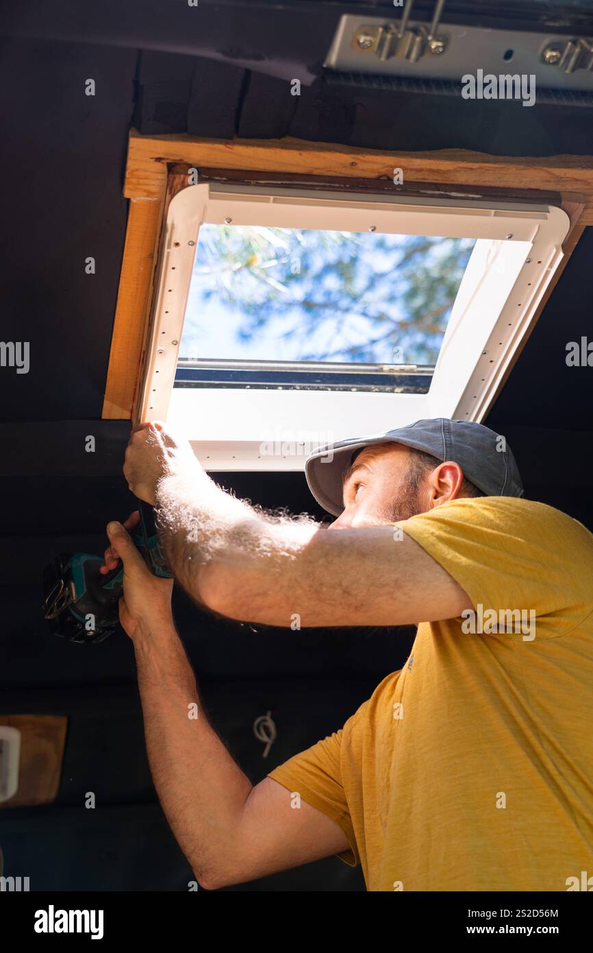 Construction worker using cordless drill to install camper van roof ...