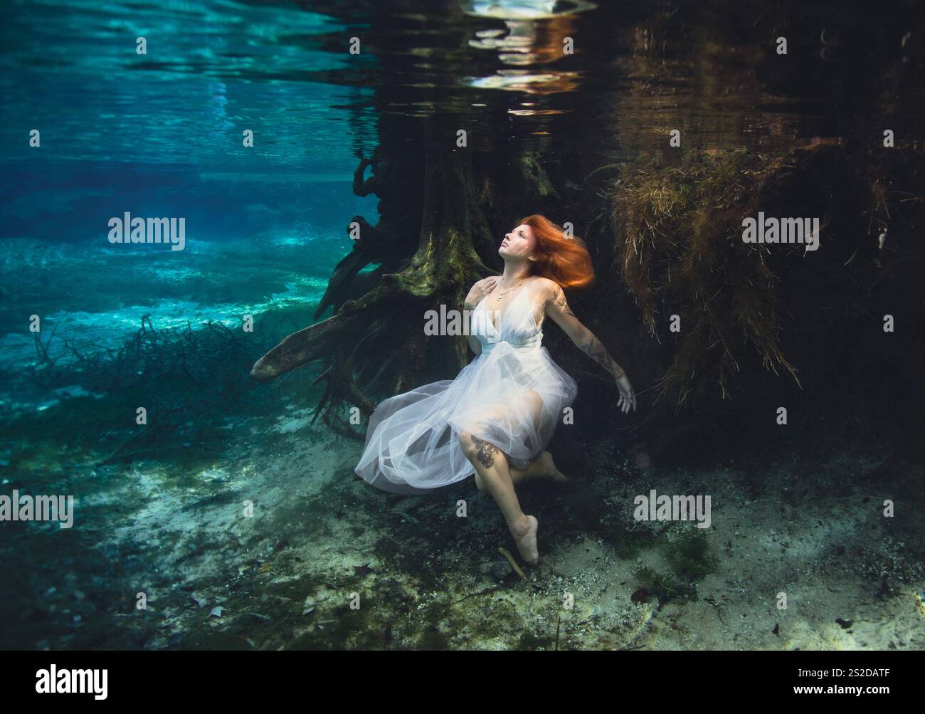 Beautiful redheaded woman in a long dress sitting underwater on a ...