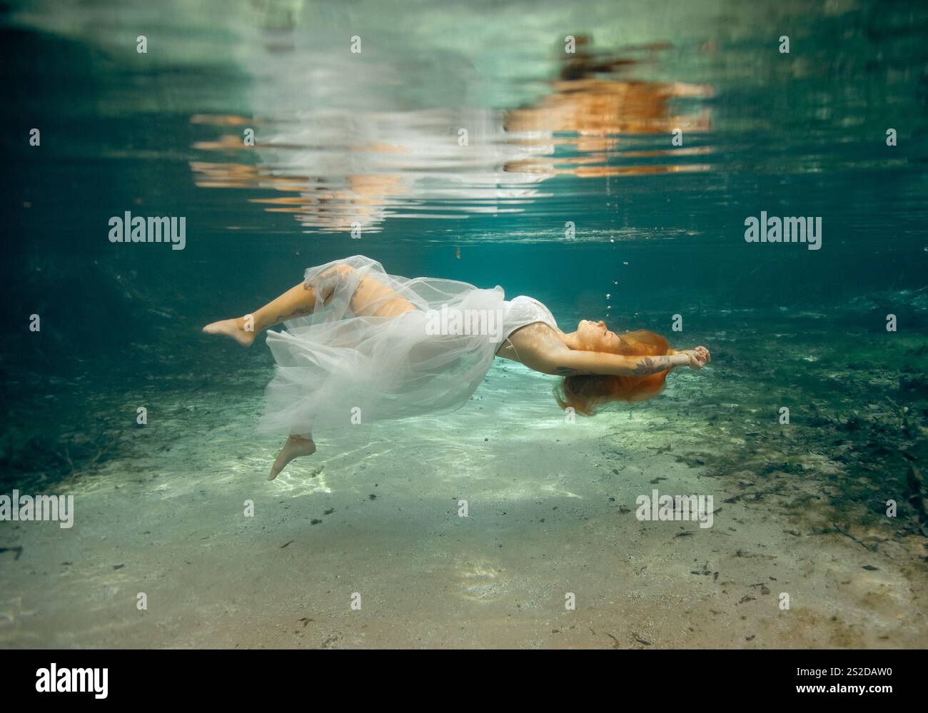 Beautiful redheaded woman in a long dress floating underwater over a ...