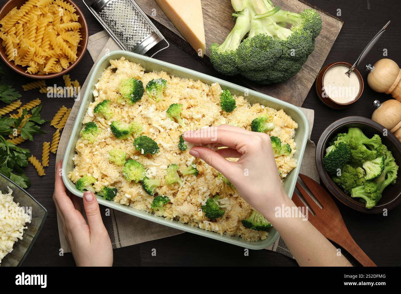 Woman adding cheese onto pasta casserole at wooden table, top view ...