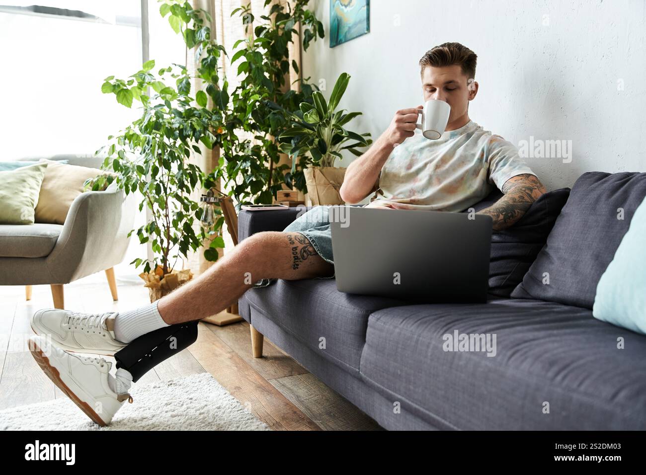 Handsome young man rests on couch with laptop, sipping coffee ...
