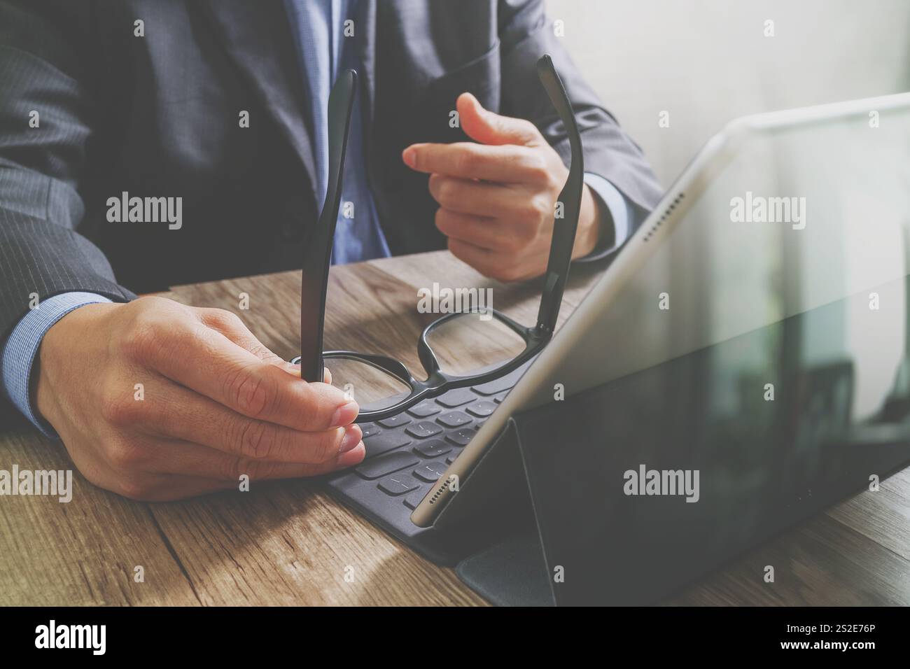 success businessman hand using eyeglass,digital tablet docking smart keyboard on wood desk ...