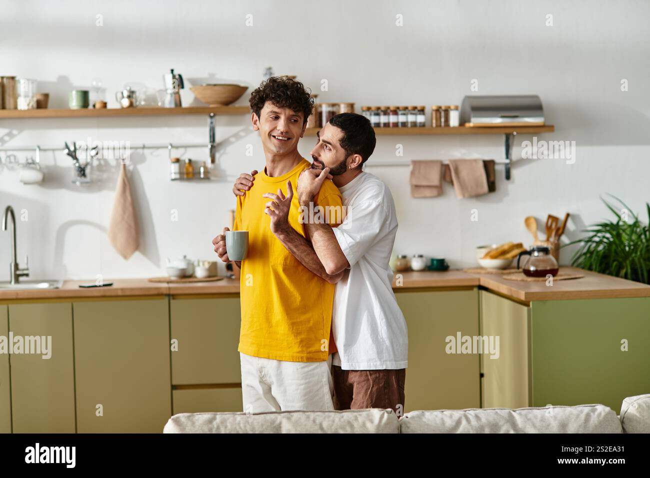 Two men embrace lovingly in their modern apartment while enjoying a ...