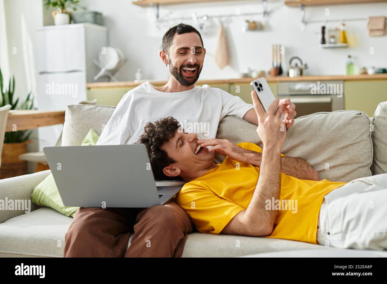Two men relax on a couch, laughing together while enjoying tech in ...