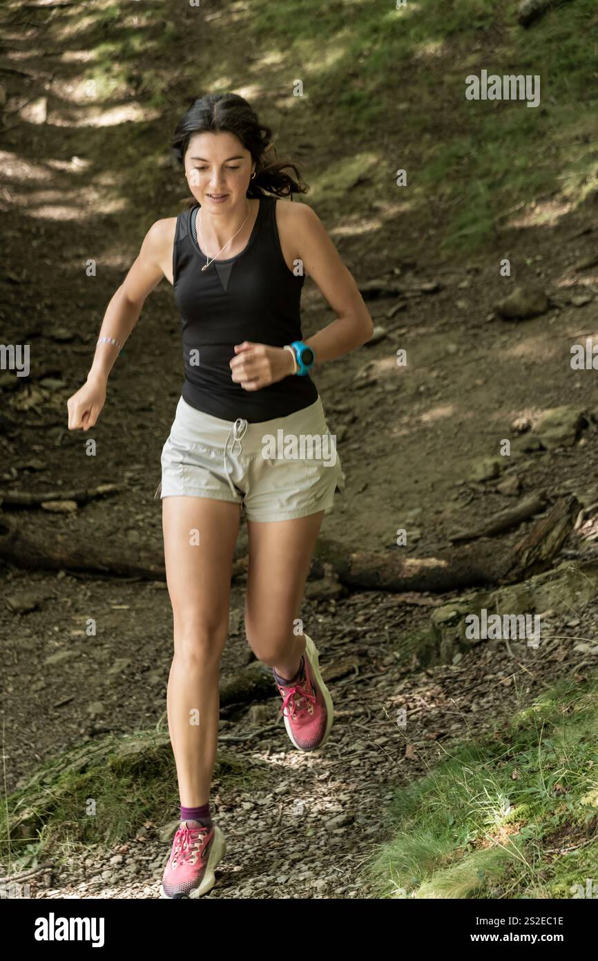 Focused woman trail running on a shaded forest path, enjoying an active ...