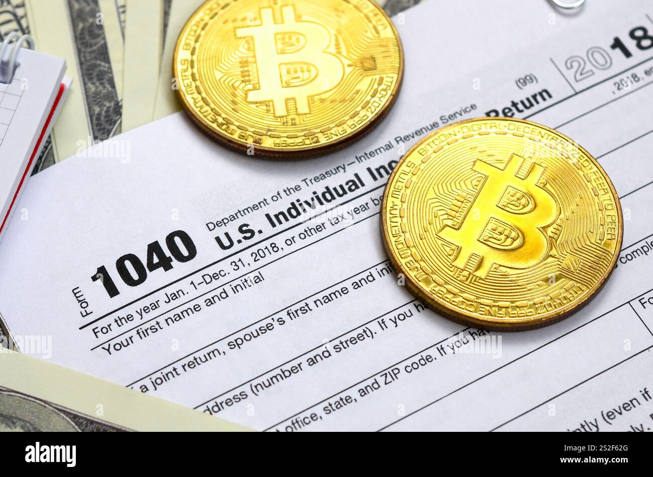 The pen, bitcoins and dollar bills is lies on the tax form 1040 U.S ...