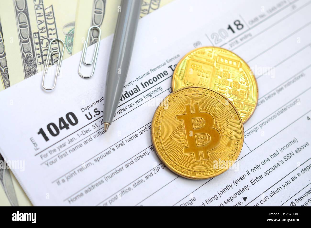 The pen, bitcoins and dollar bills is lies on the tax form 1040 U.S ...