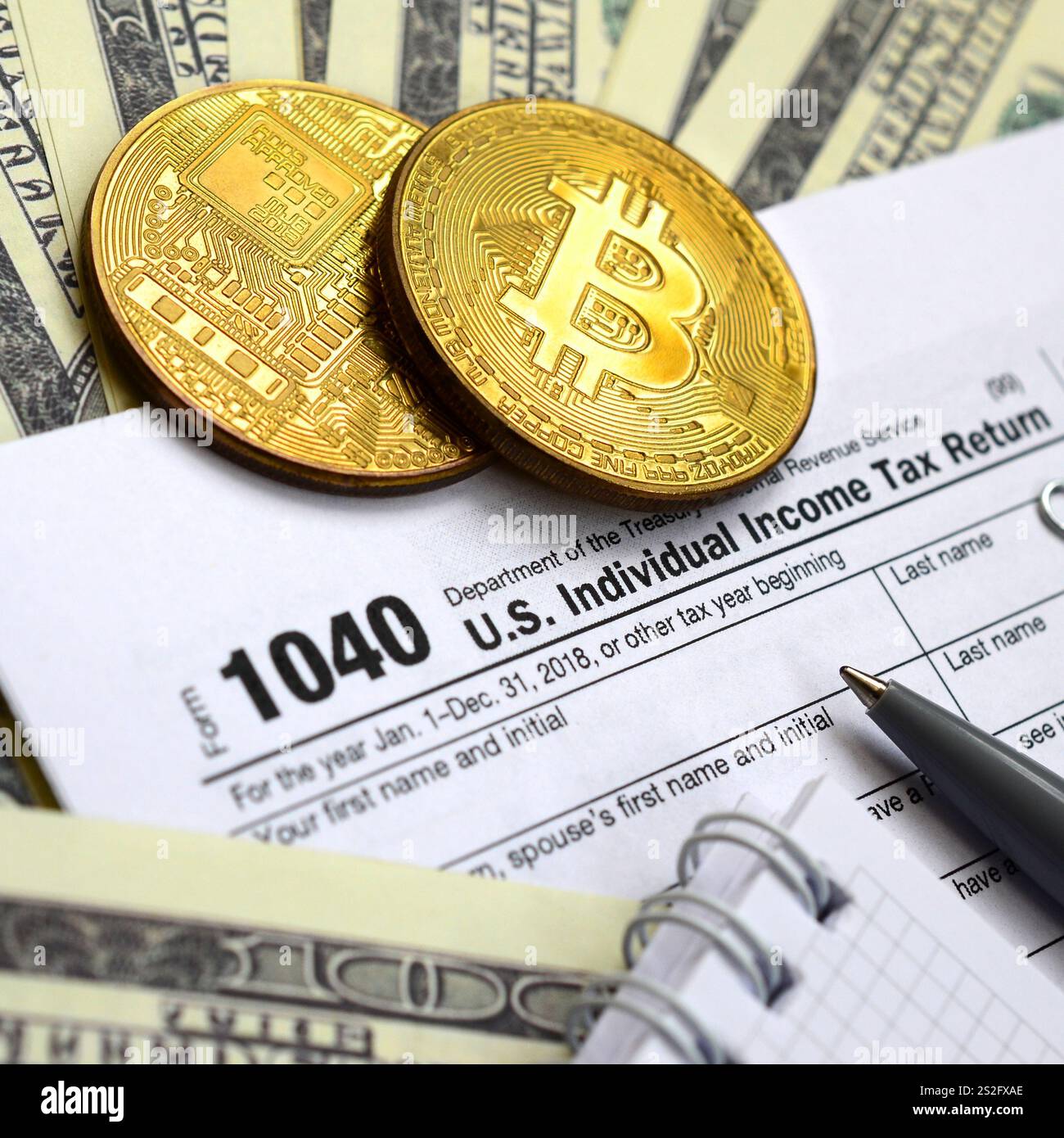 The pen, bitcoins and dollar bills is lies on the tax form 1040 U.S ...