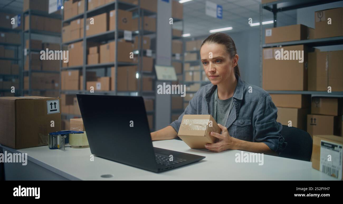 Female post office worker scans cardboard parcel using barcode scanner, enters data on laptop ...