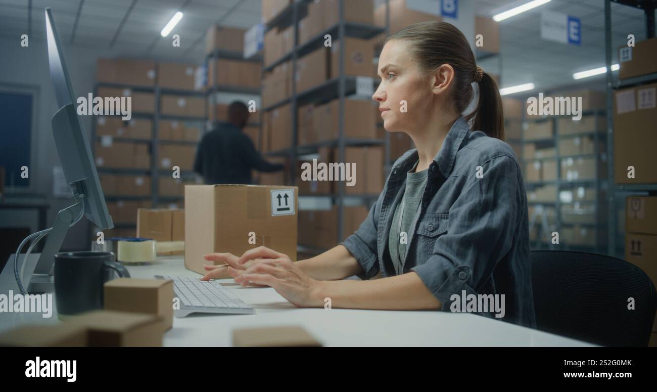 Female warehouse clerk scans parcel with barcode scanner, uses computer, works in postal service ...