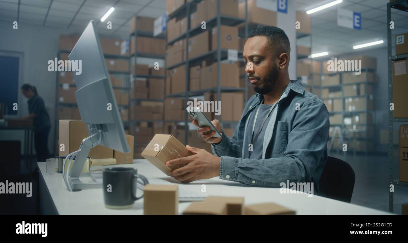 African American logistics manager scans parcel using smartphone, works in post office warehouse ...