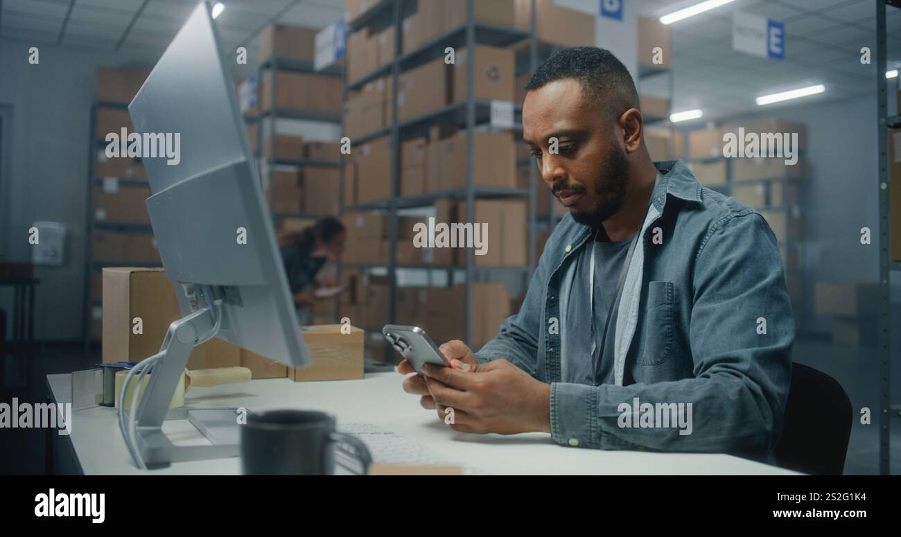 African American logistics manager scans parcel using smartphone, works in post office warehouse ...