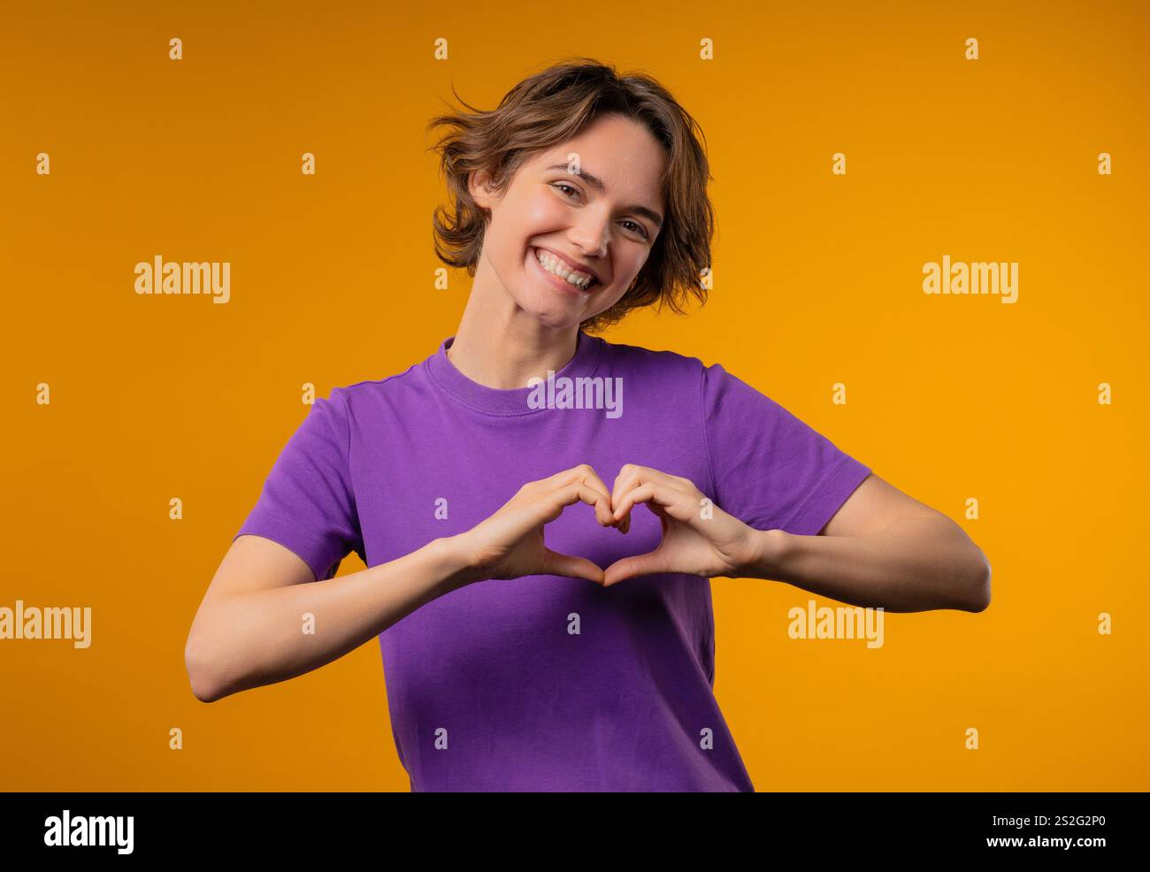 Smiling woman showing sign of shape heart. Positive lady on yellow ...