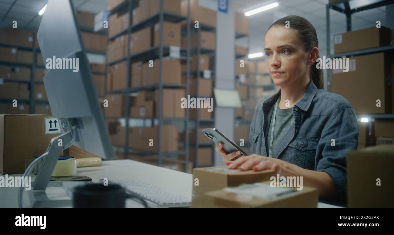 Female inventory clerk scans parcel using smartphone, enters data on computer, works with E ...