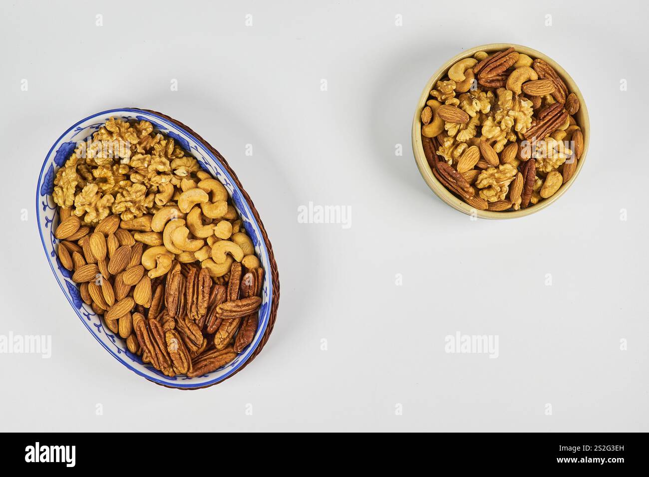 Assorted nuts in a stoneware container with a straw basket, on a white ...