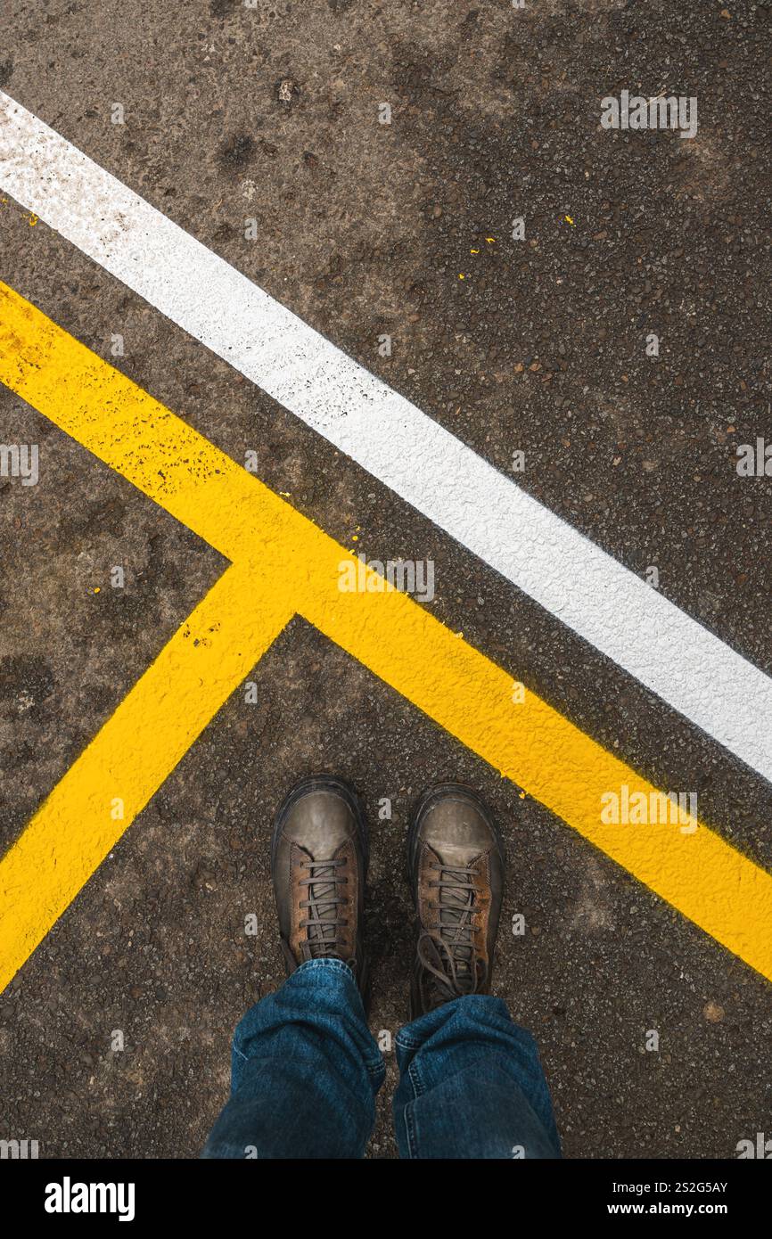 Male boots from above, man standing on asphalt road with yellow and ...