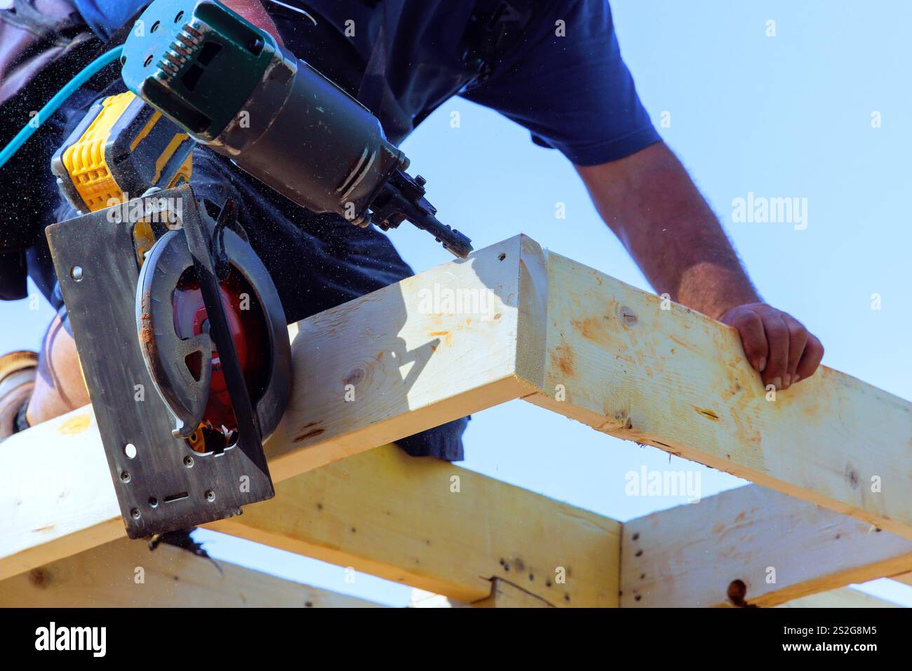 Construction worker uses pneumatic nail gun air tool to secure wooden beams while working on ...