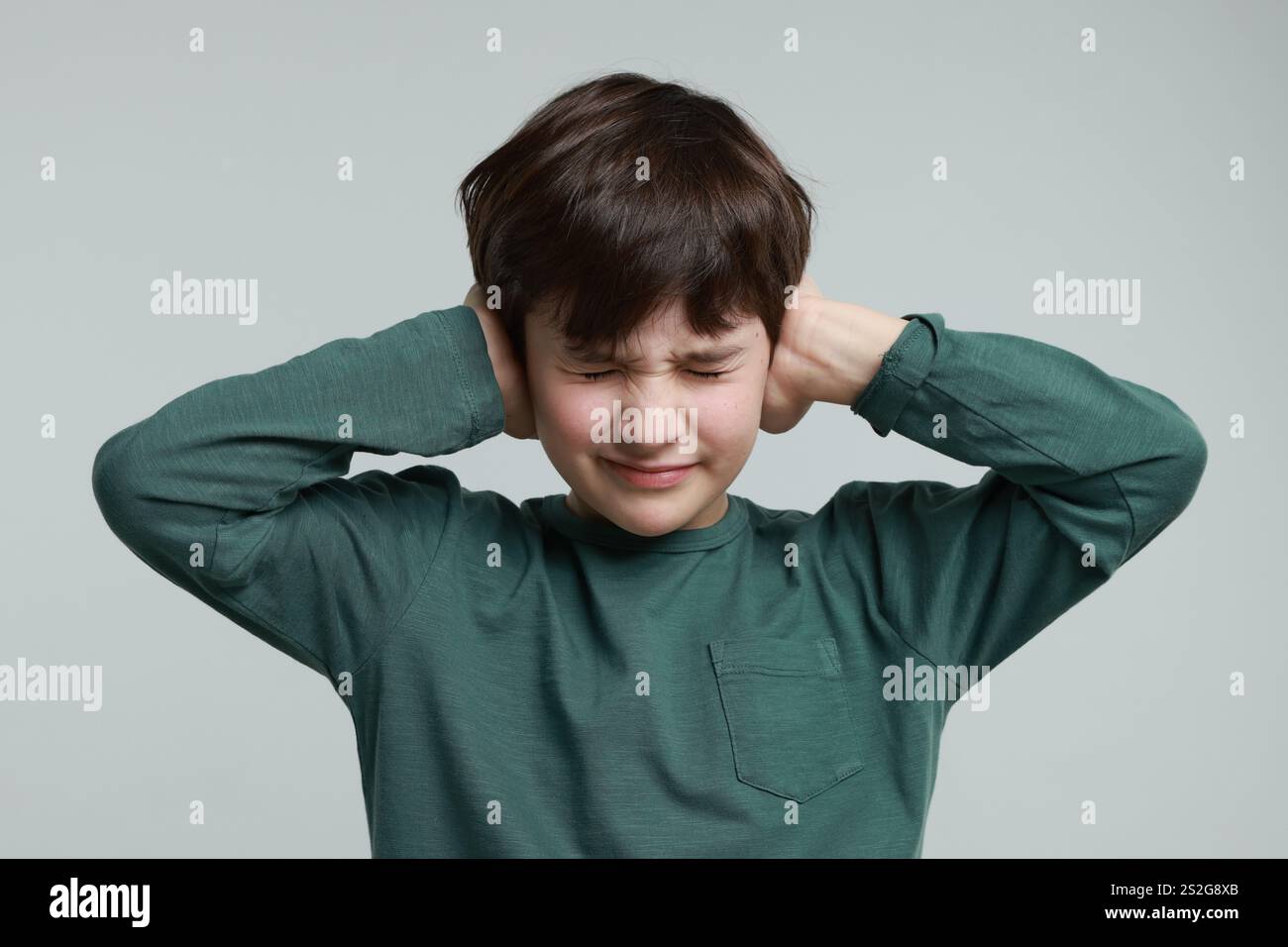 Annoyed boy covering his ears due to loud sound on grey background ...