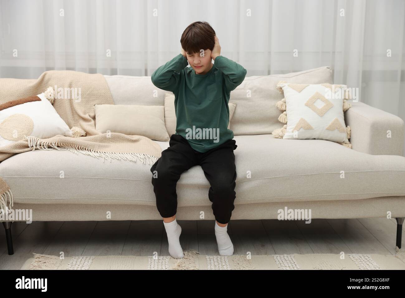 Annoyed boy covering his ears due to loud sound on sofa at home Stock ...