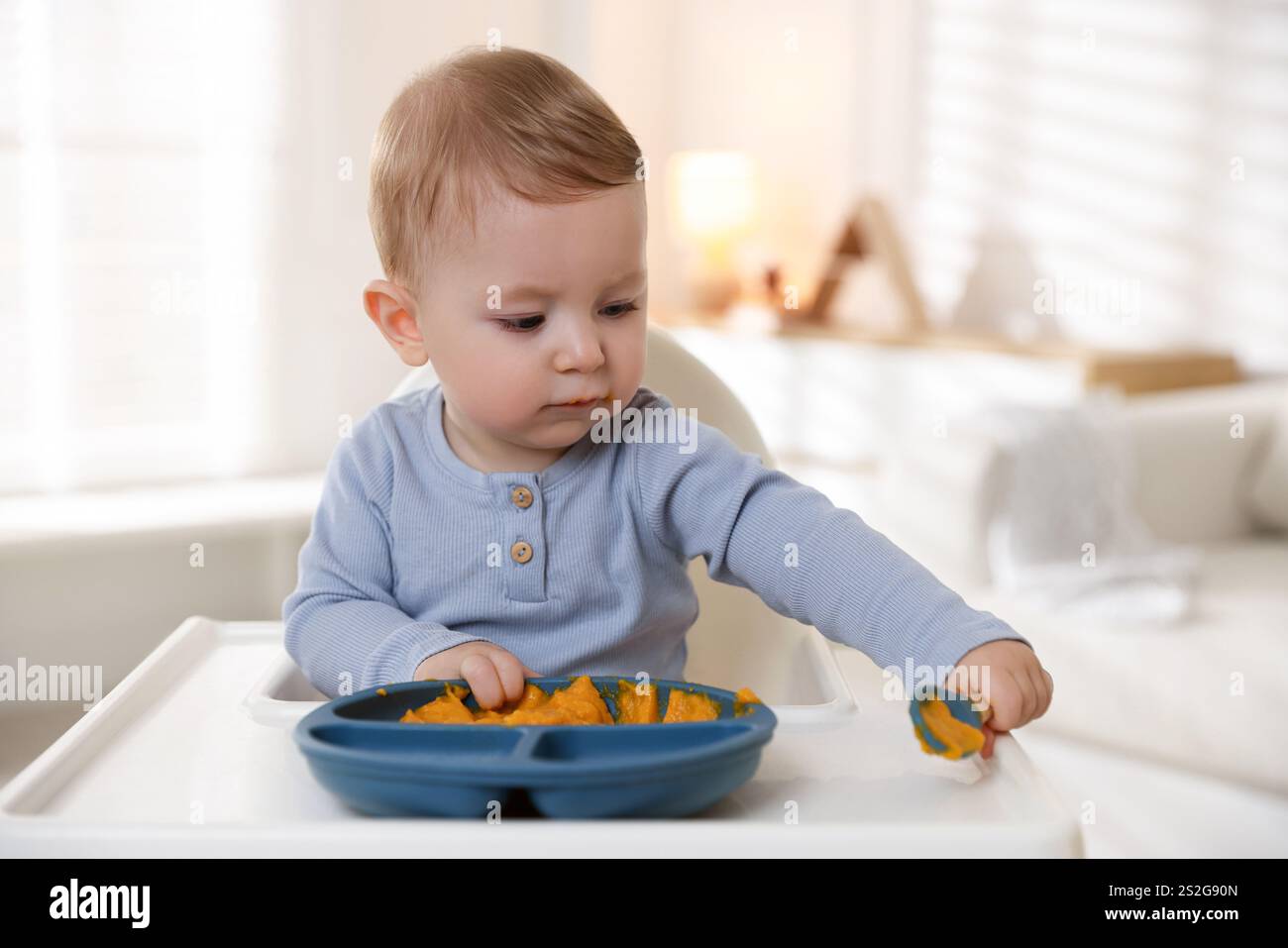 Cute little baby eating healthy food in high chair indoors Stock Photo ...
