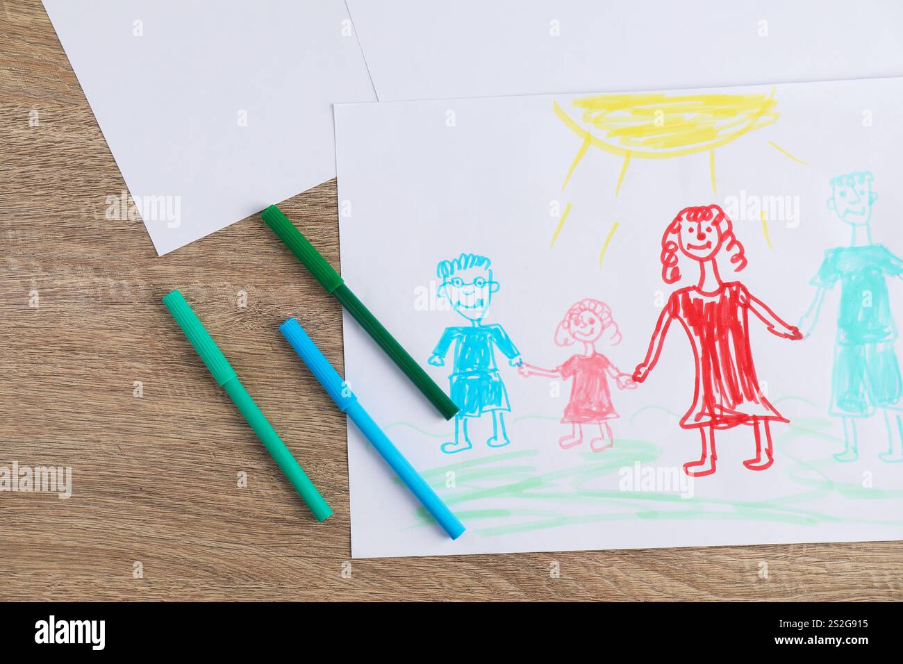 Child's drawing of happy family and felt tip pens on wooden table, top ...