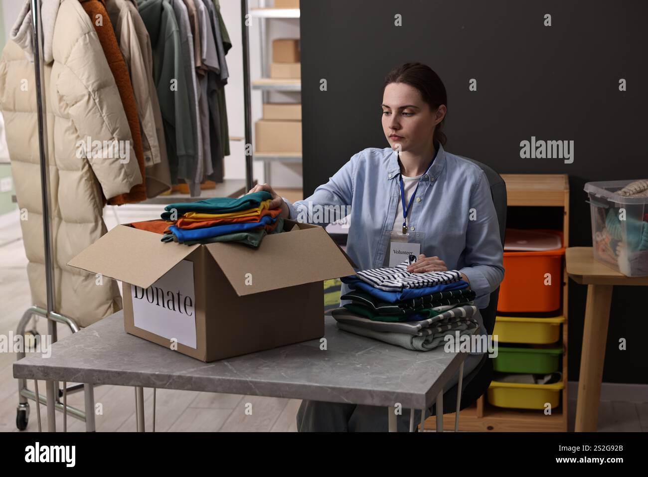 Volunteer putting clothes into donation box at table indoors Stock ...