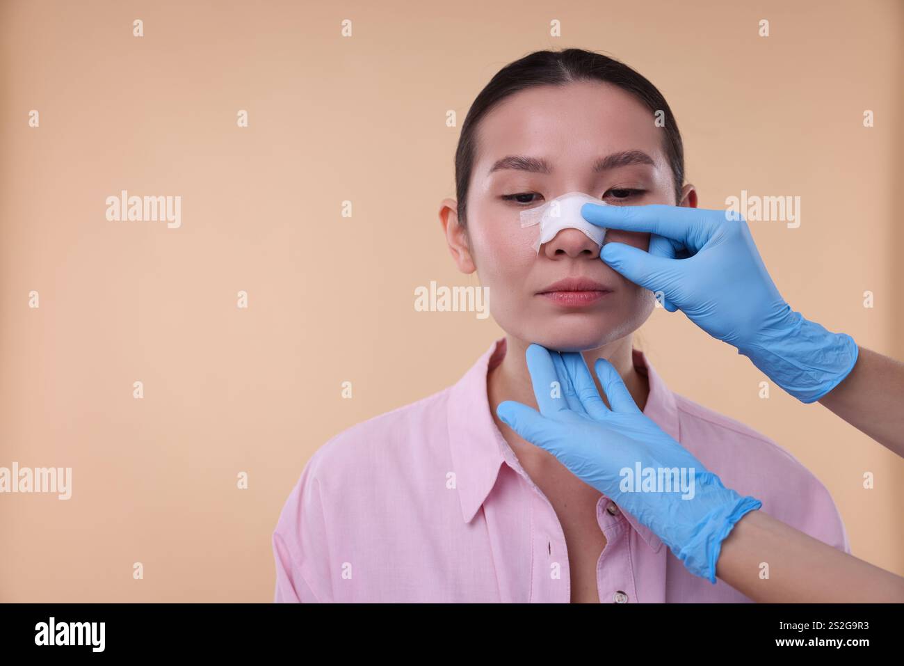 Doctor checking patient's nose after plastic surgery operation on beige ...