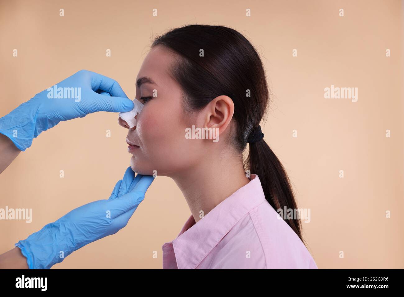 Doctor checking patient's nose after plastic surgery operation on beige ...