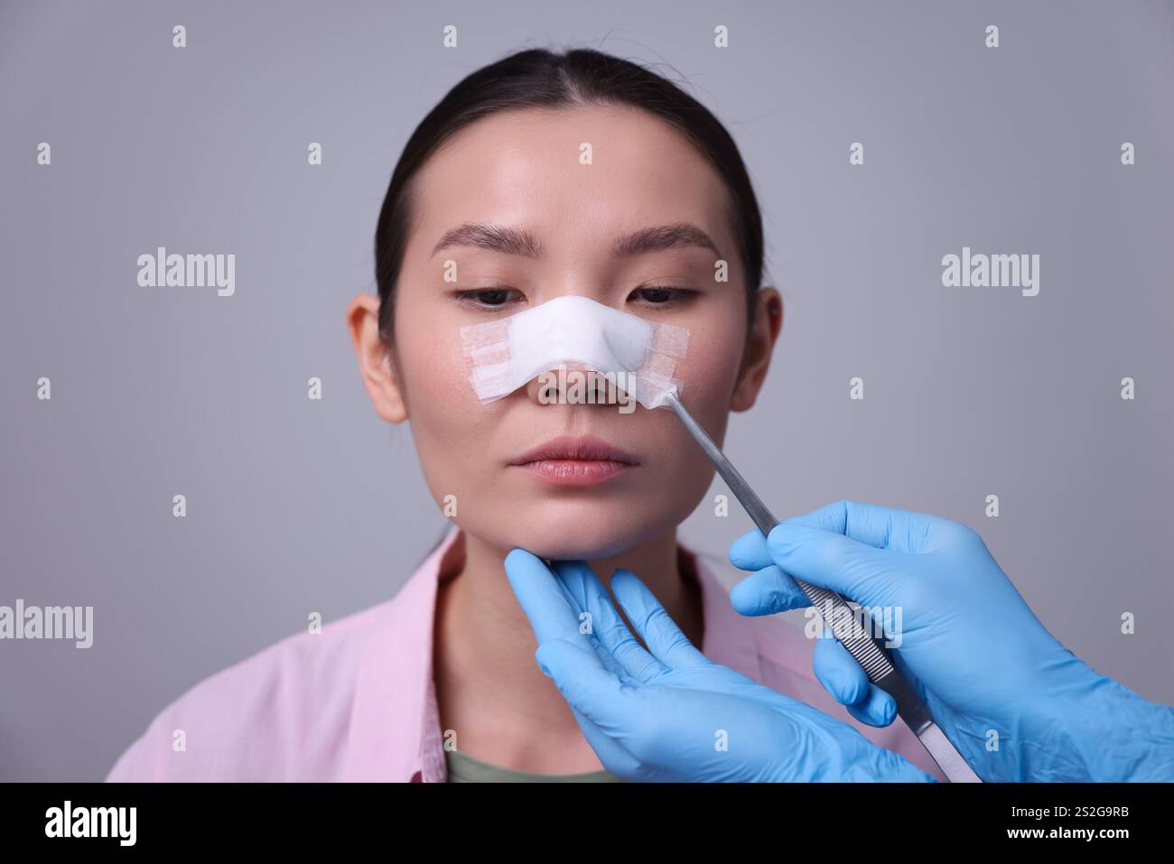 Doctor removing medical bandage from patient's nose after plastic surgery operation on light ...
