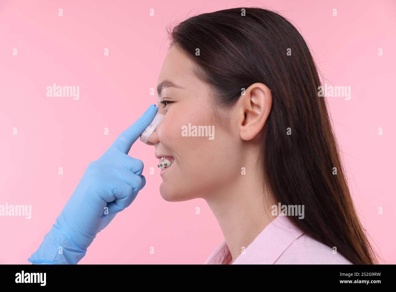 Doctor checking patient's nose after plastic surgery operation on pink ...