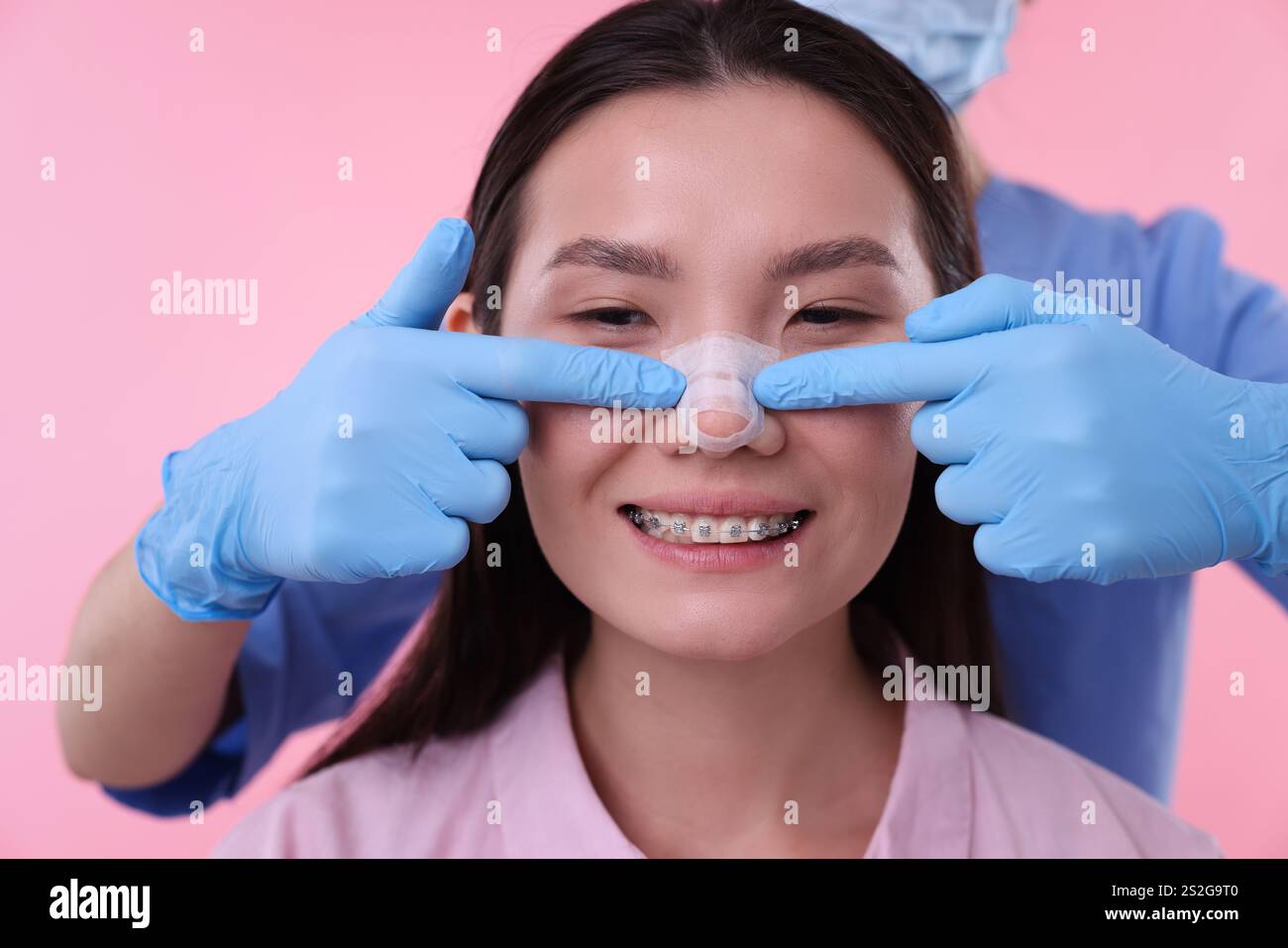 Doctor checking patient's nose after plastic surgery operation on pink ...