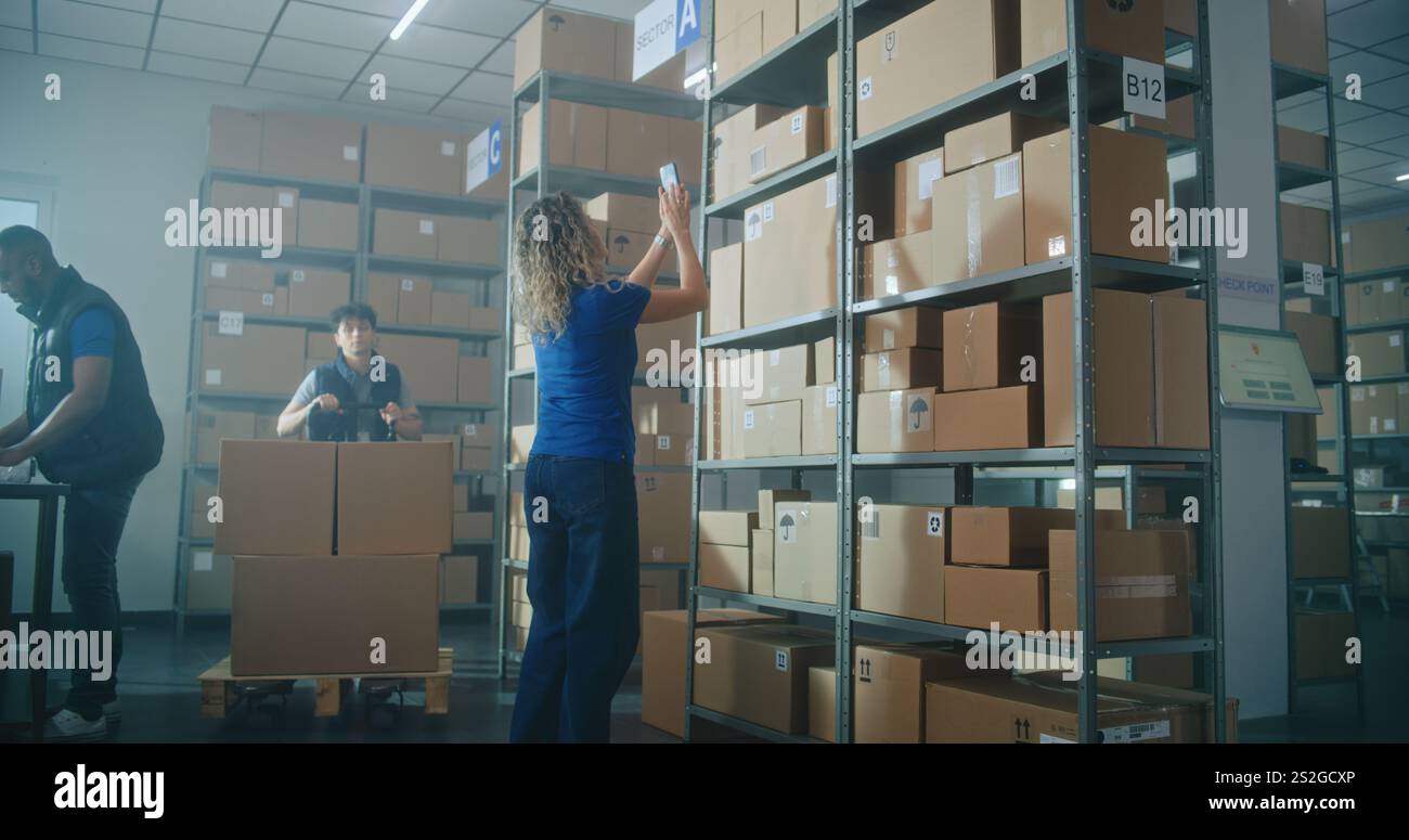 Female logistics specialist scans code on cardboard box using smartphone. Male warehouse worker ...