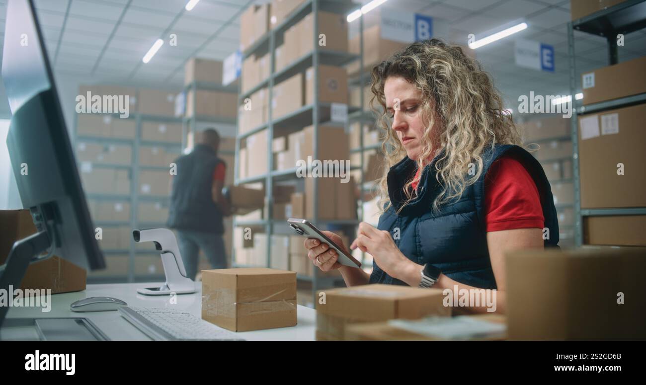 Female logistics manager scans small parcels using smartphone, works in warehouse of postal ...