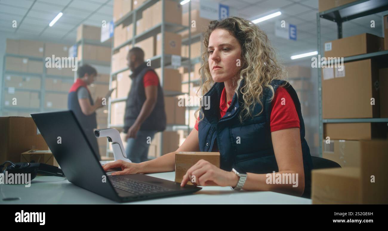 Female logistics specialist scans parcel with barcode scanner, checks data using laptop. Sorting ...