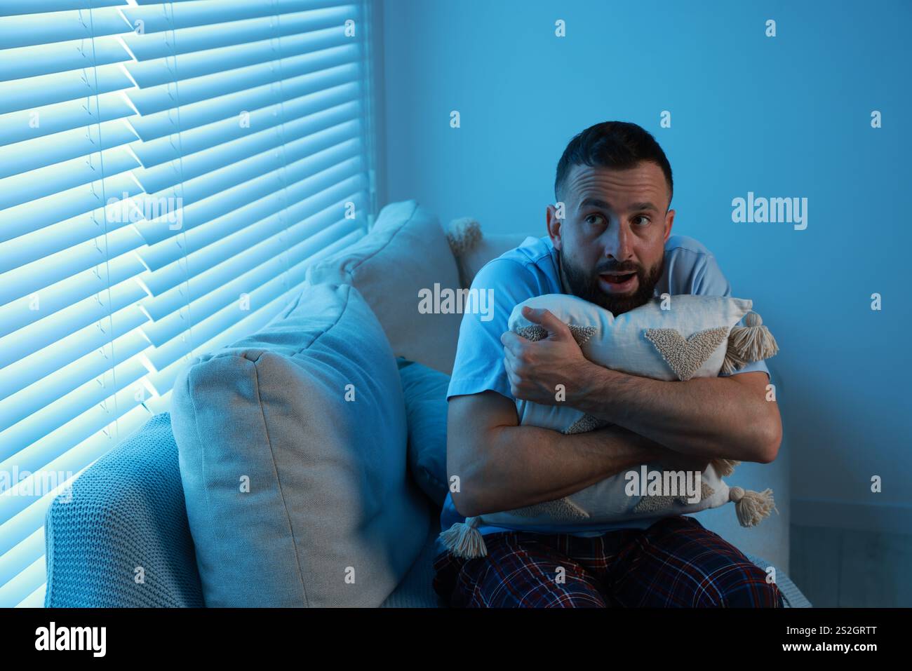 Fear of darkness. Scared man hugging pillow on couch in dark room ...