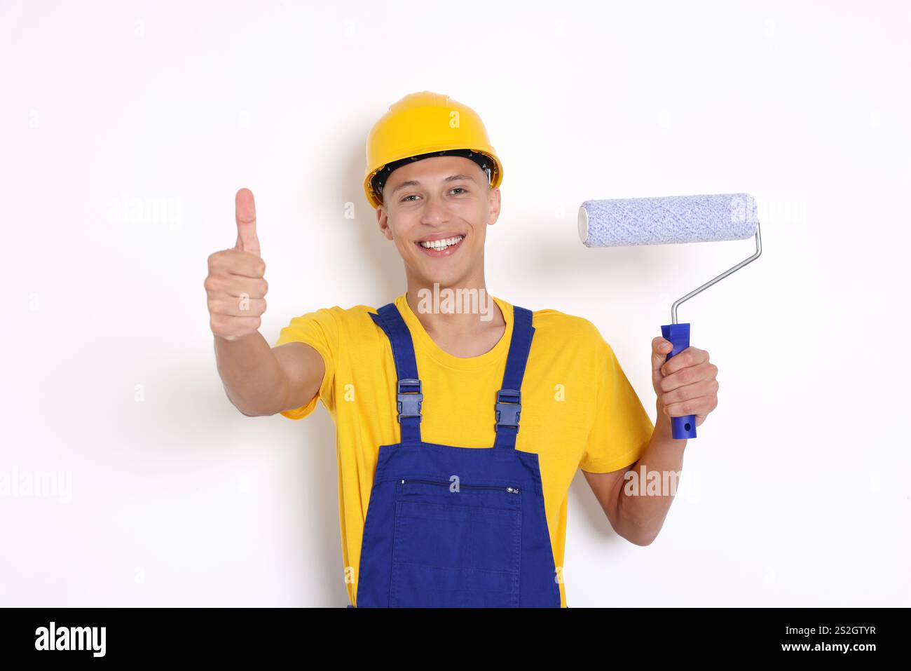Portrait of young decorator with paint roller showing thumbs up on ...