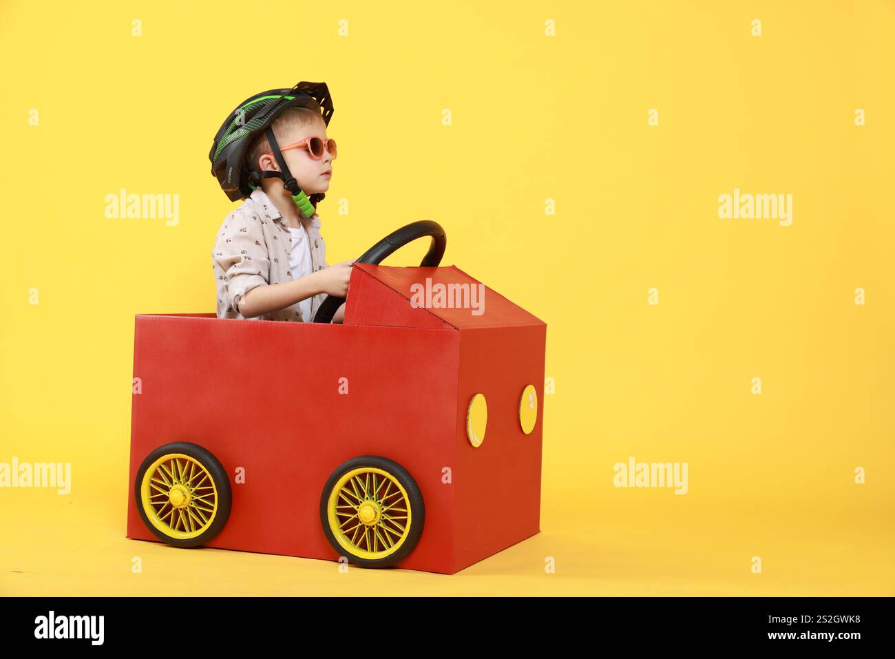 Little boy driving car made of cardboard on yellow background. Space ...