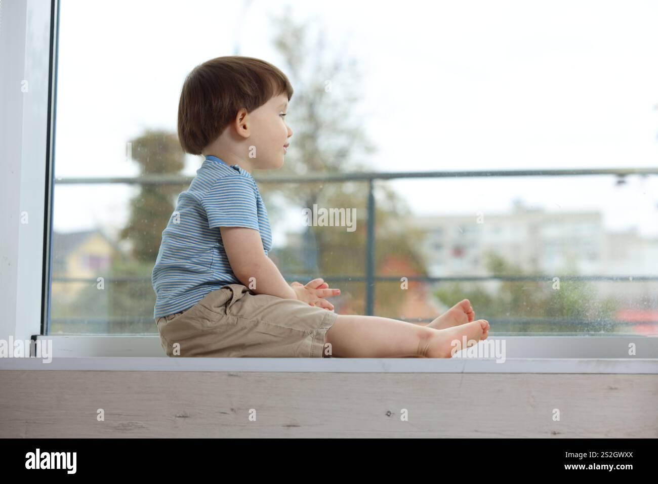 Little boy sitting on window sill. Child in danger Stock Photo - Alamy