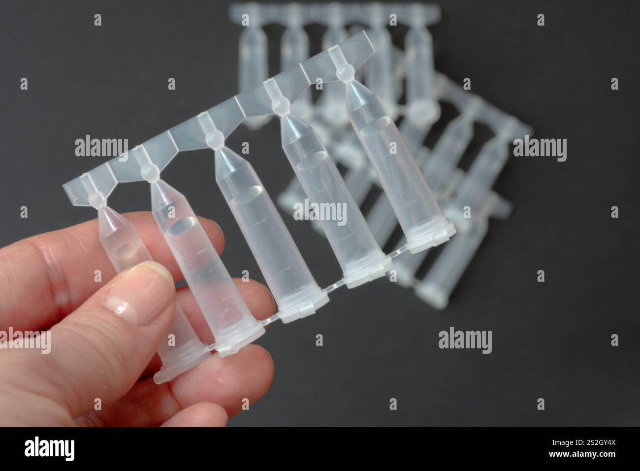 Hand Holding disposable eye drops against dark background. Pack of eye ...