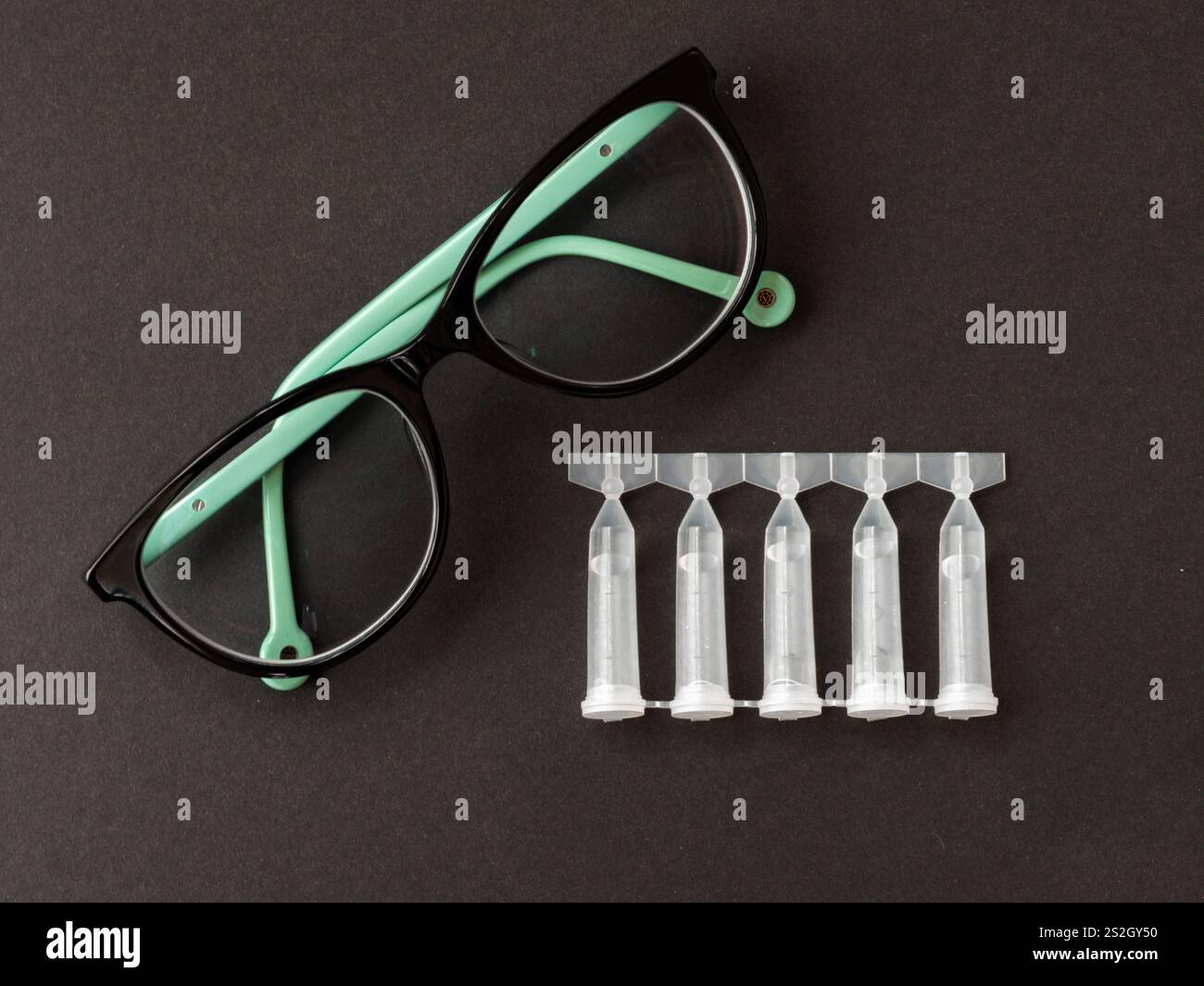 Black and green eyeglasses and disposable eye drops isolated on dark ...