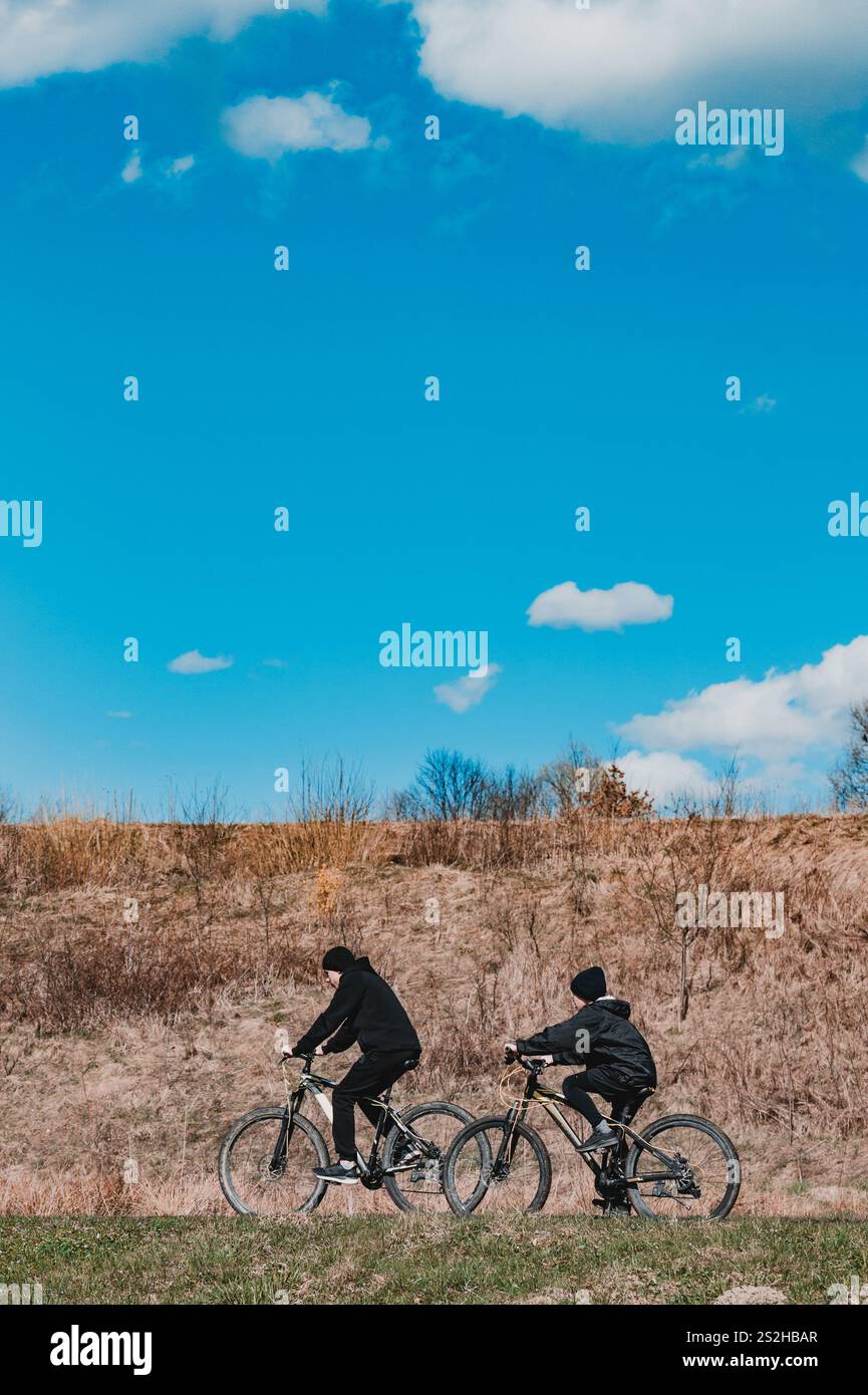 Two individuals in black clothing cycle side by side on a path against ...