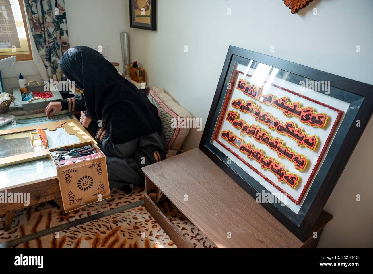 A calligraphy frame crafted with quilling paper is displayed next to ...