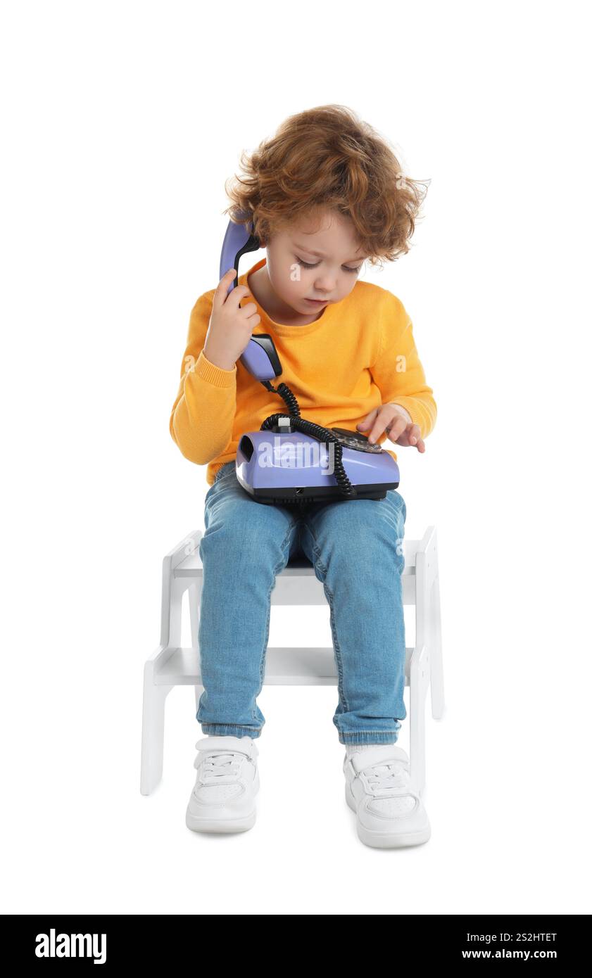 Cute little boy with telephone on step stool against white background ...