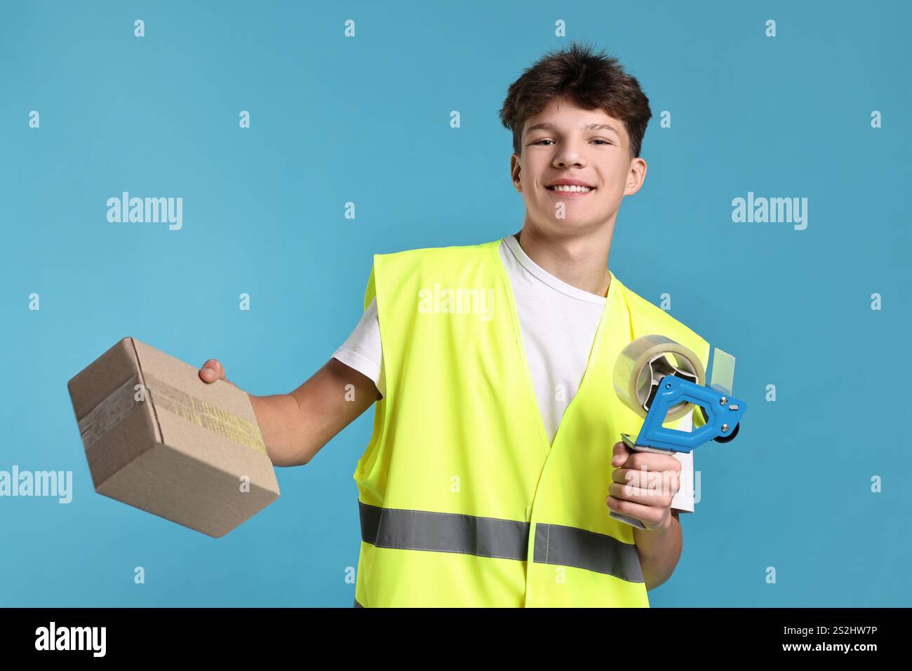 Teenage boy with tape gun dispenser and box in safety vest working as ...