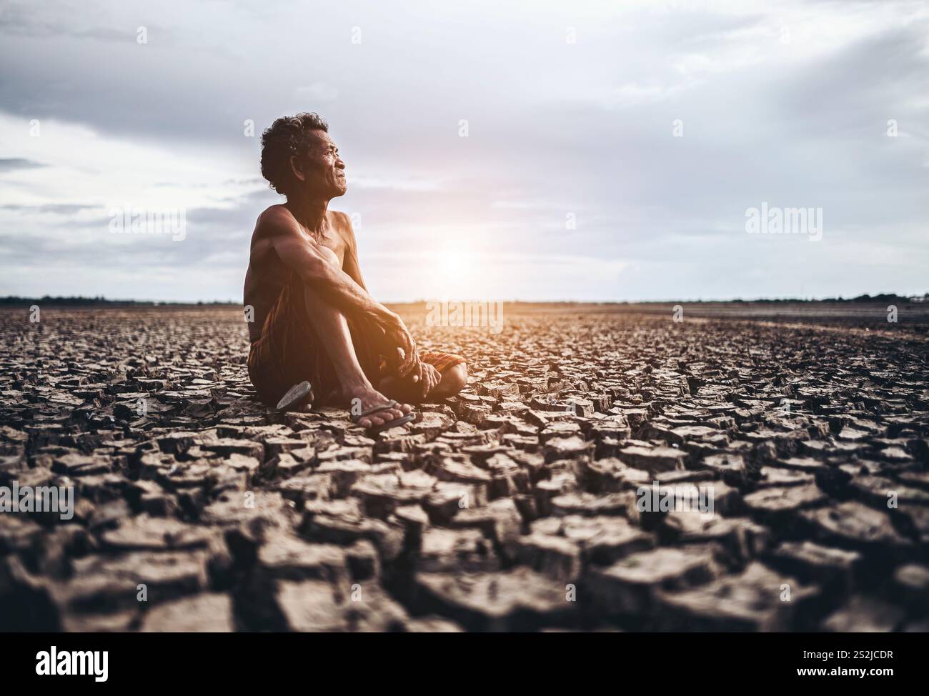 An elderly man sat hugging his knees bent on dry soil and looked at the ...