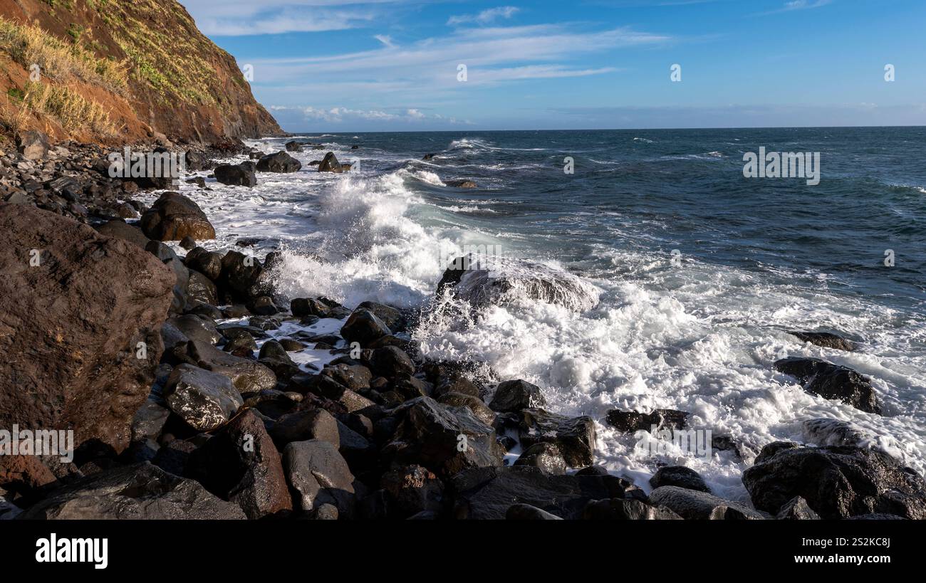 Rocky coastline with waves crashing against black rocks under a clear ...