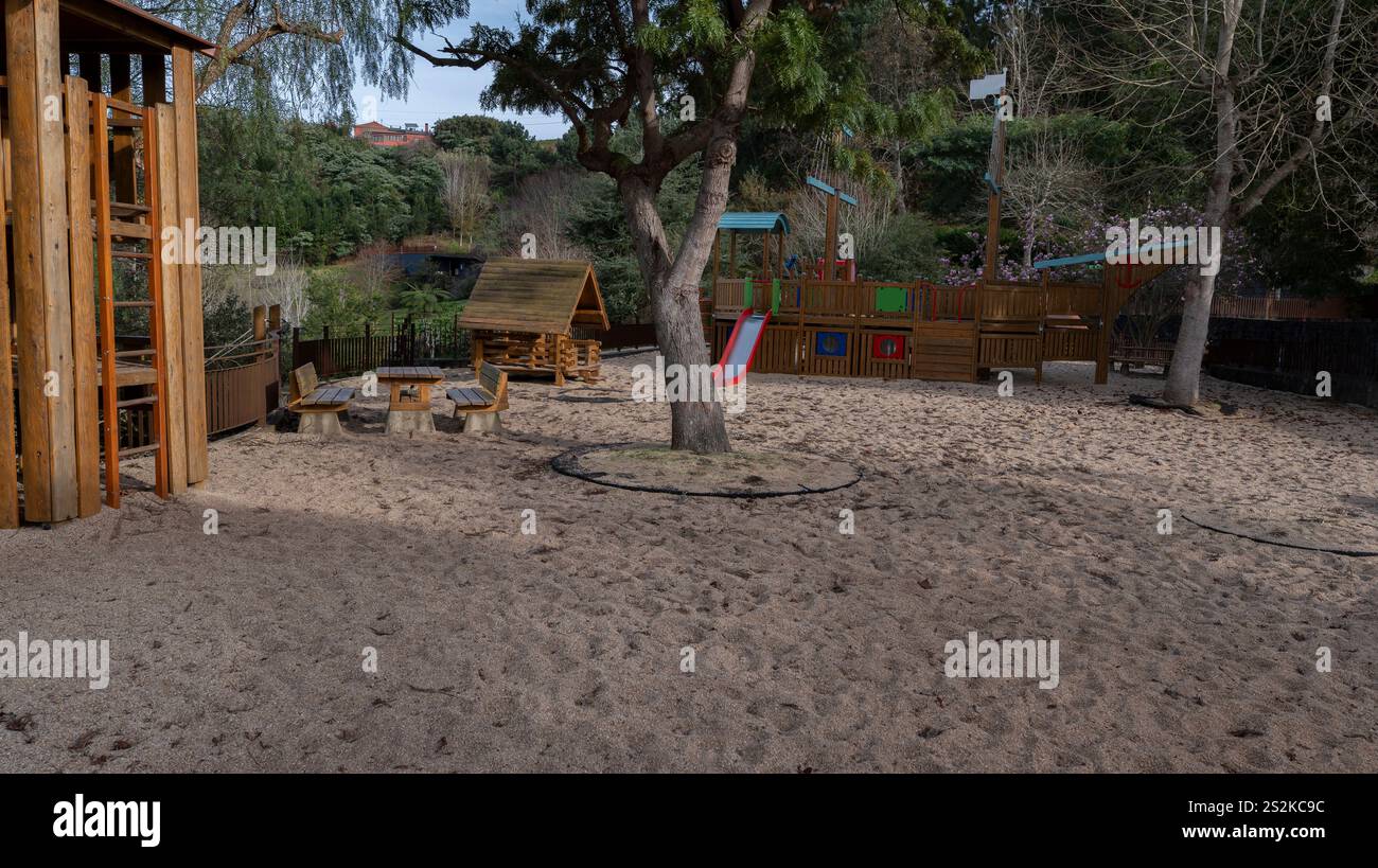 A playground with wooden structures, a slide, and sand-covered ground ...