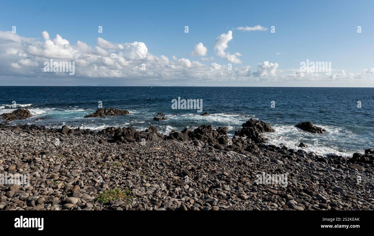 A rocky shoreline with dark pebbles and scattered rocks extending into ...