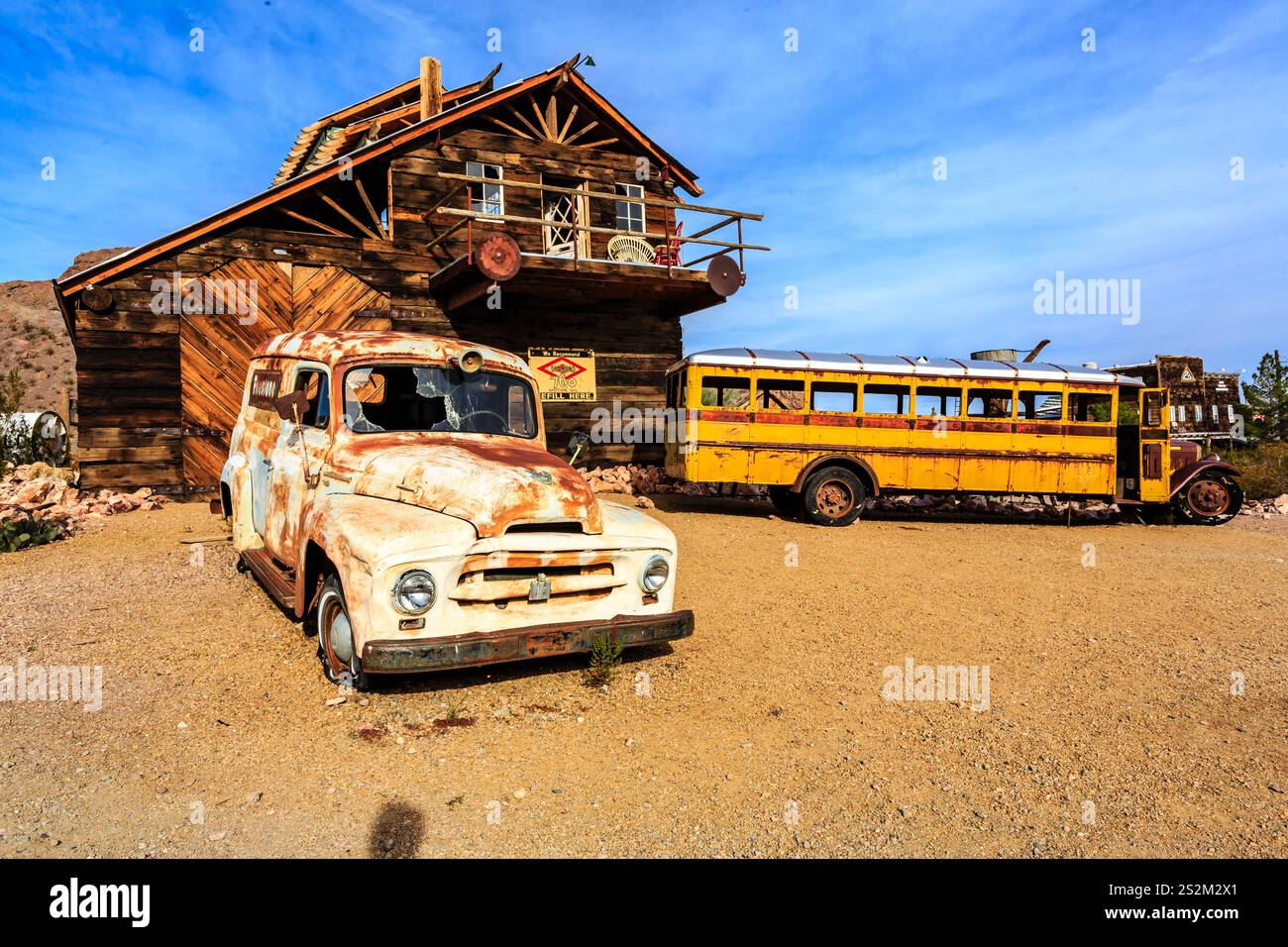 An old bus and a truck are parked in front of a rustic building. The ...